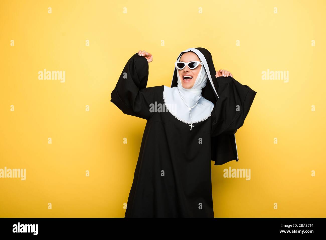 attractive happy emotional nun dancing in sunglasses on yellow Stock ...