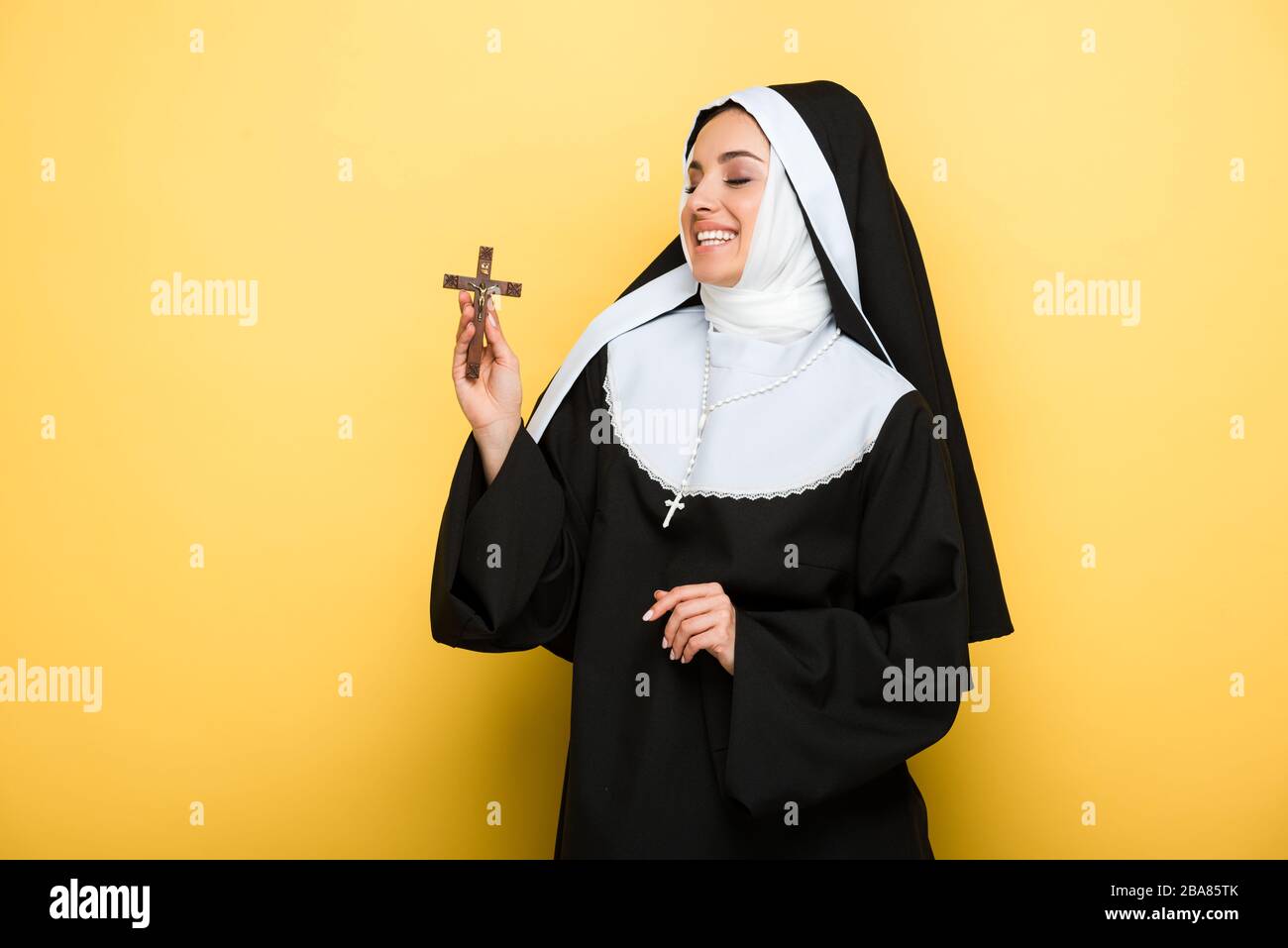 beautiful cheerful nun holding cross on yellow Stock Photo - Alamy