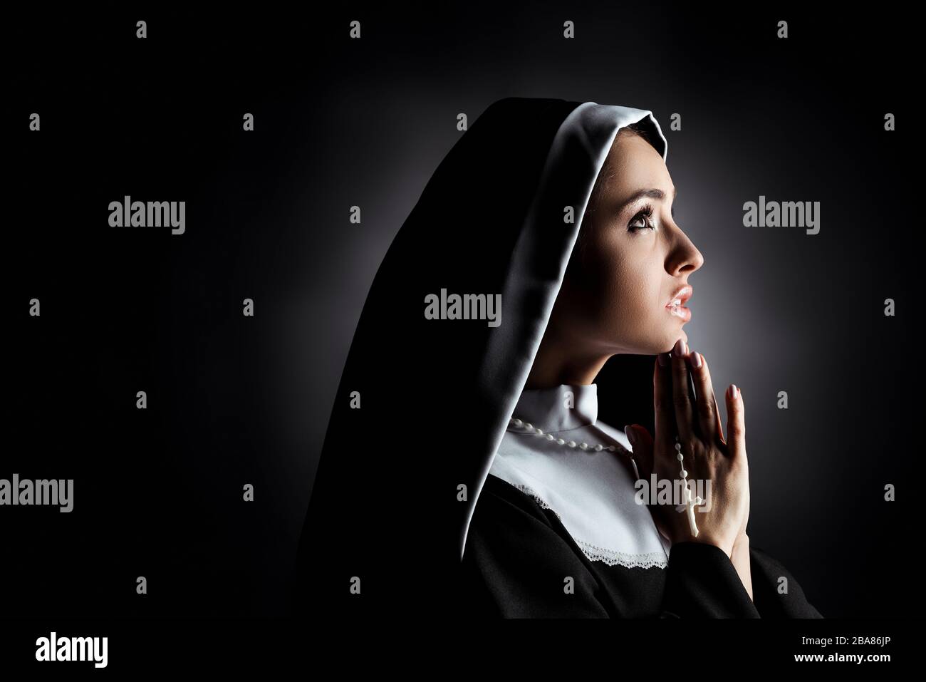 beautiful young nun looking up while praying with cross on grey Stock ...