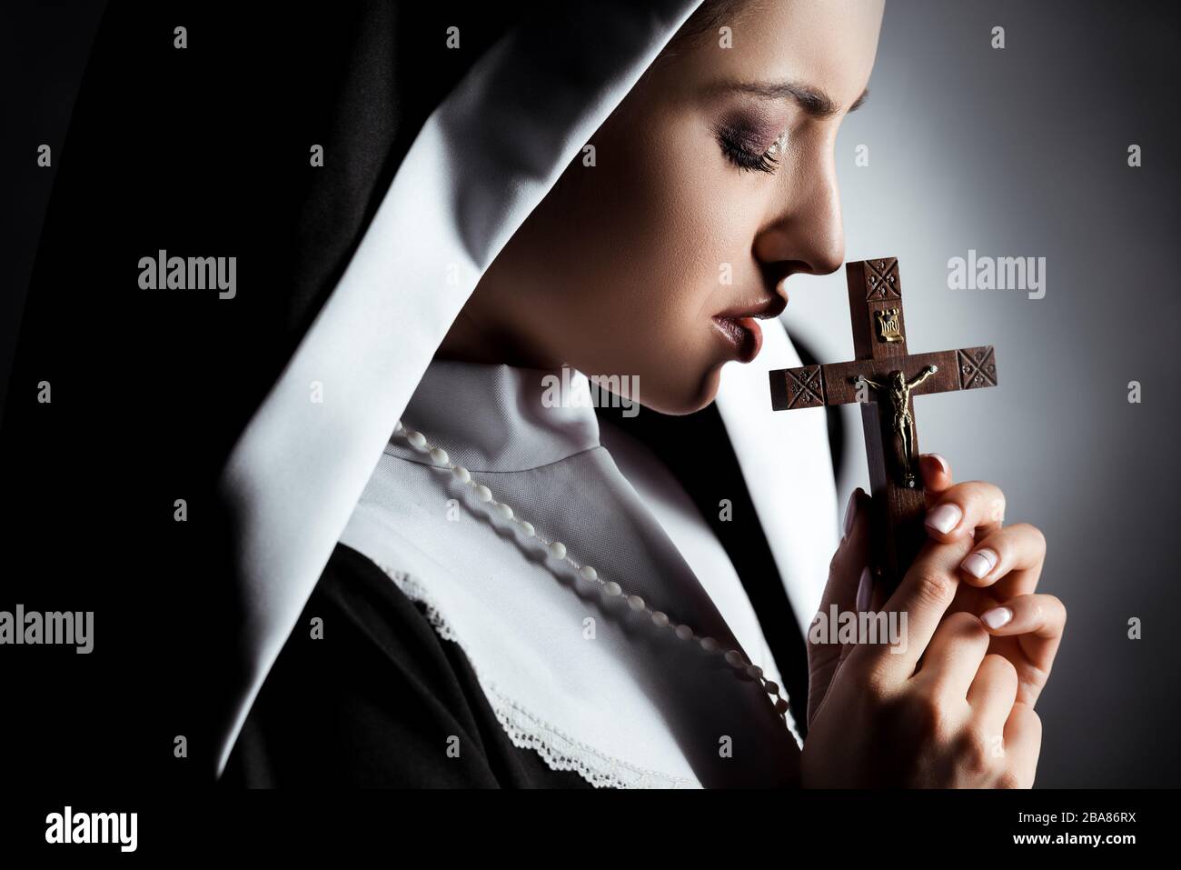 sad young nun praying with cross on grey Stock Photo - Alamy