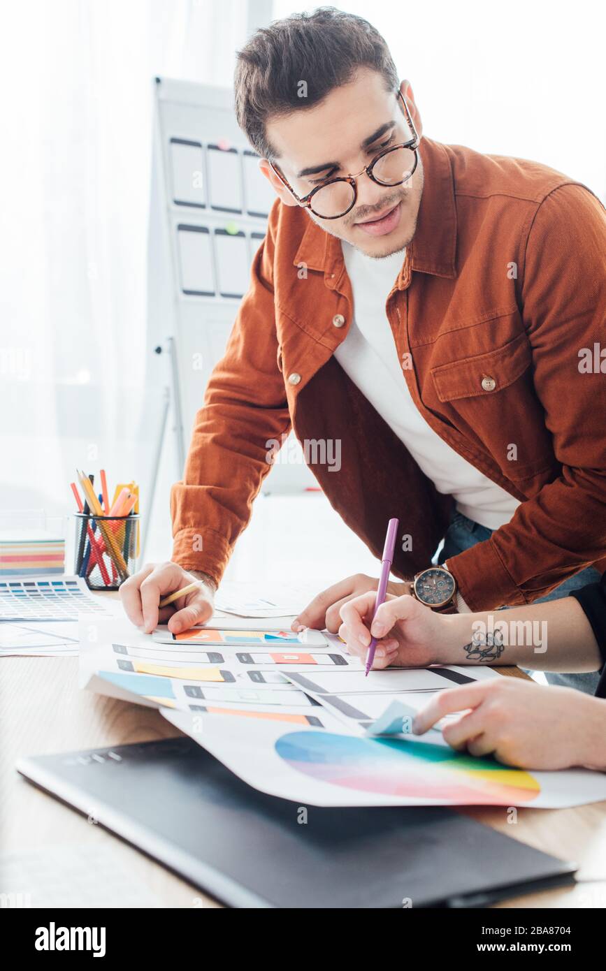 Designer looking at colleague with framework layouts of user experience ...