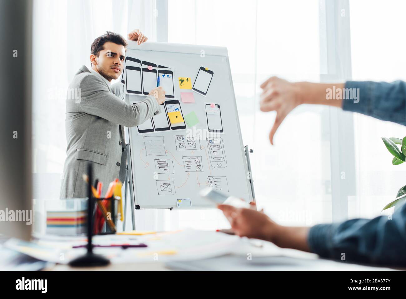 Selective focus of sad ux designer near whiteboard with layouts looking ...