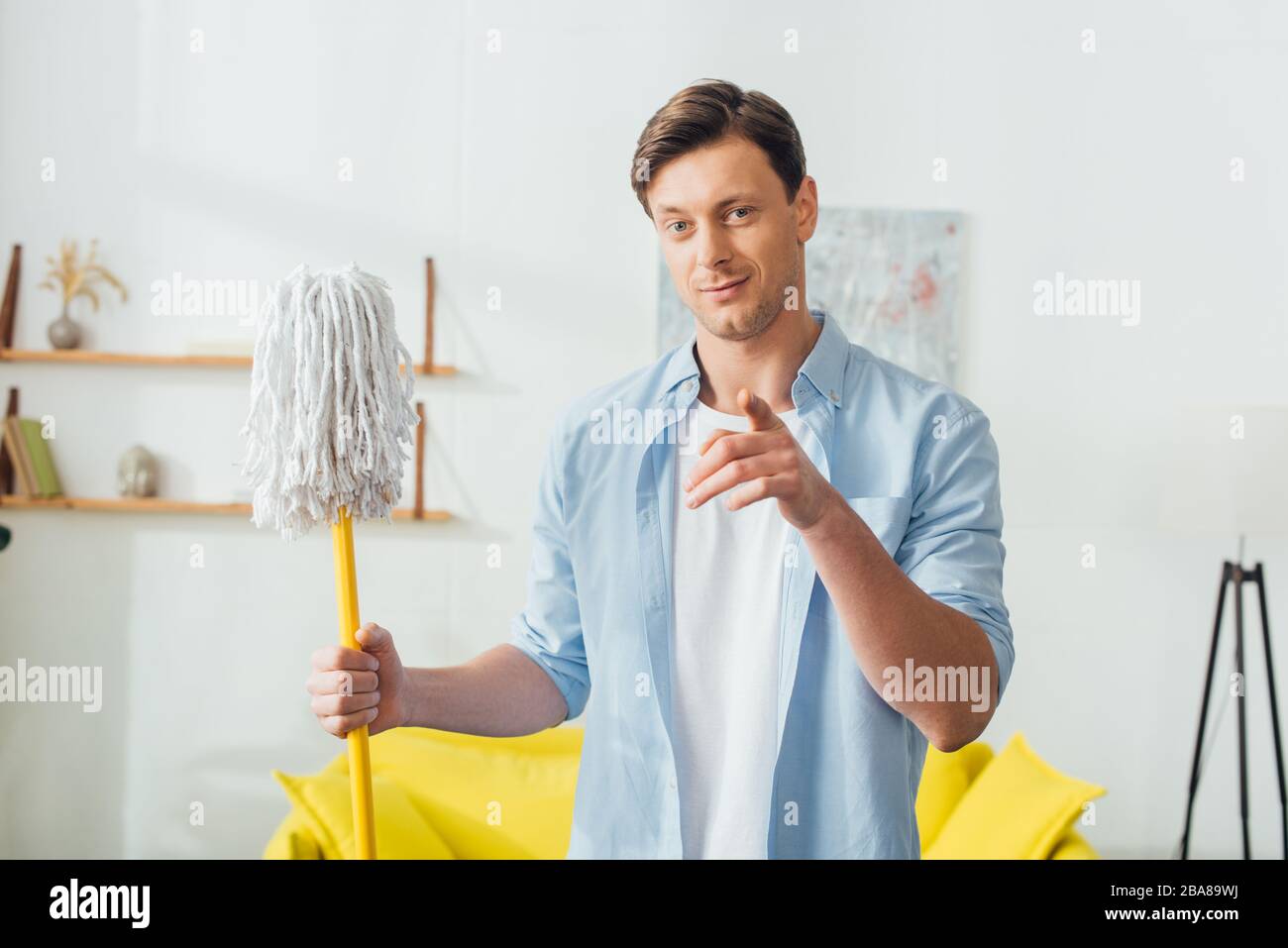 Handsome man pointing at camera and holding mop in living room Stock ...