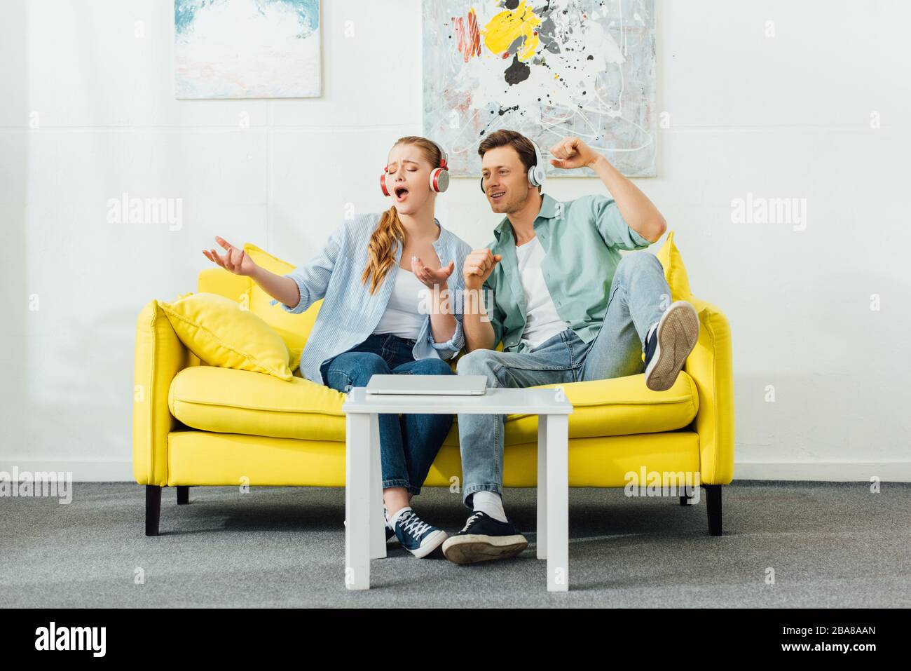 Girl singing near boyfriend in headphones on couch in living room Stock ...
