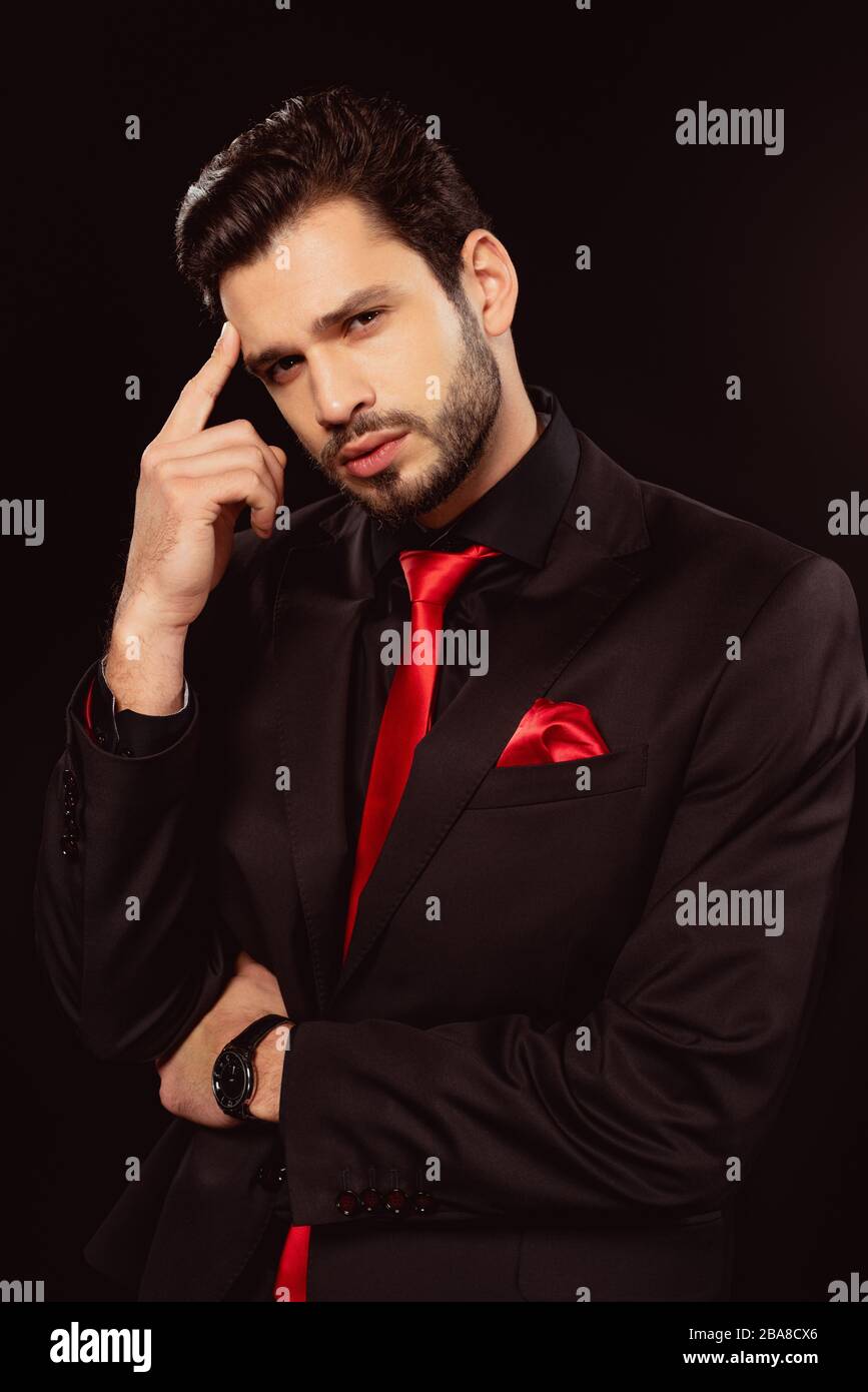 Handsome man in suit and red tie looking at camera isolated on black ...