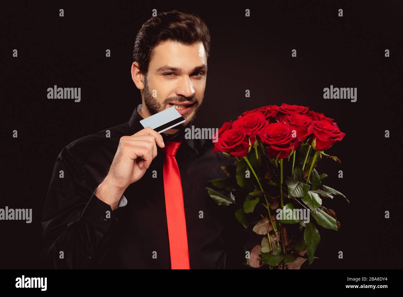 Handsome man biting credit card and holding bouquet of roses isolated ...