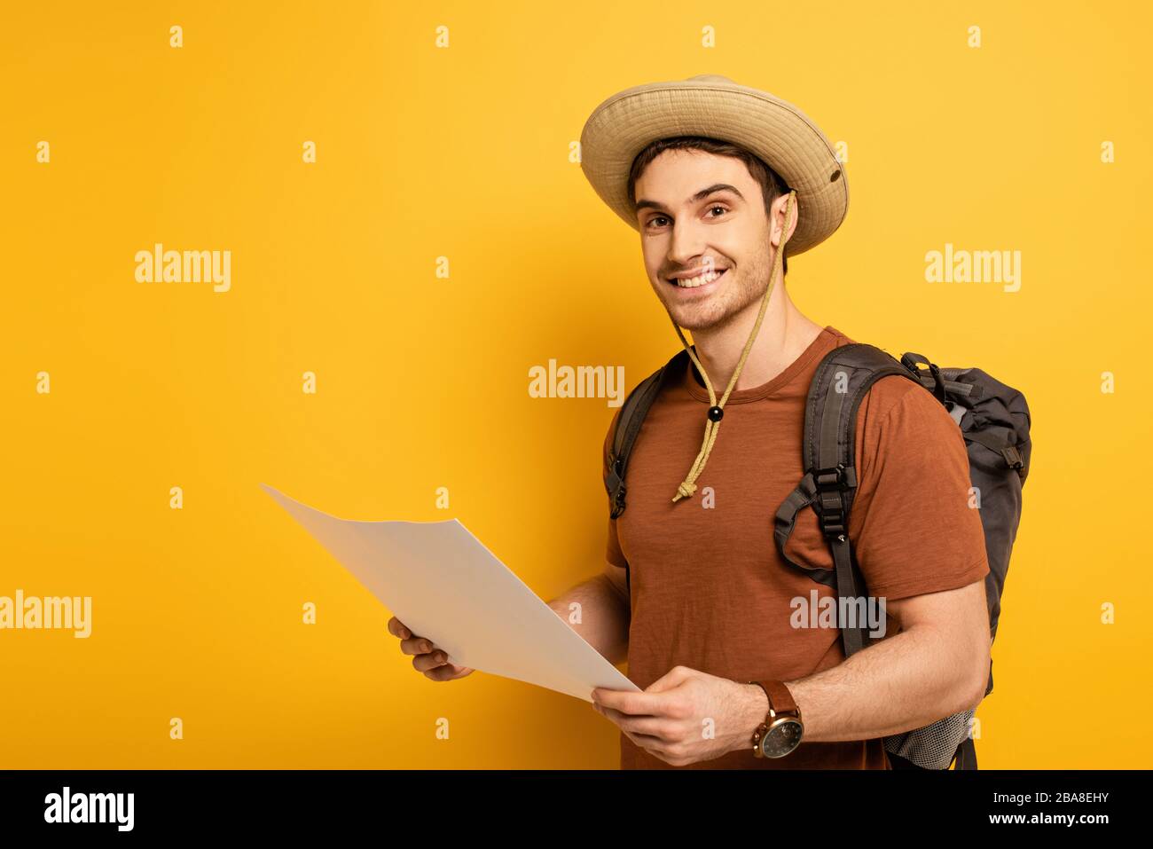 handsome smiling tourist in hat with backpack holding map on yellow ...