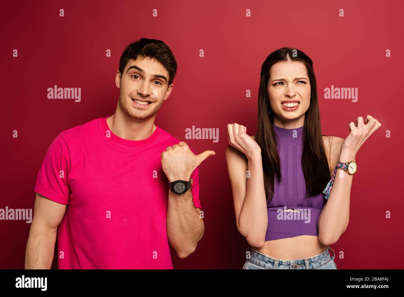 smiling boyfriend showing confused girlfriend on red Stock Photo - Alamy