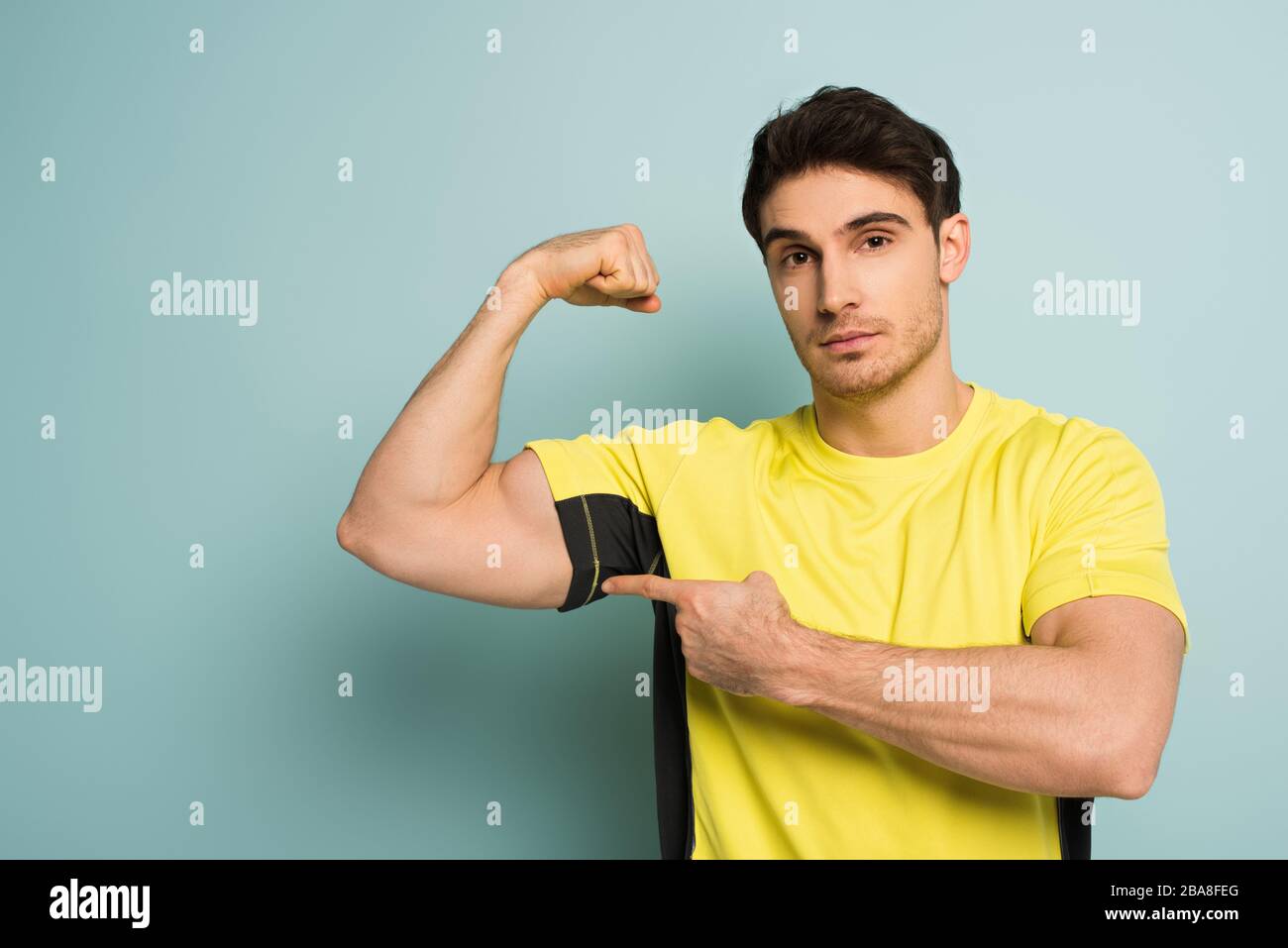muscular sportsman in yellow t-shirt pointing at muscles on blue Stock ...