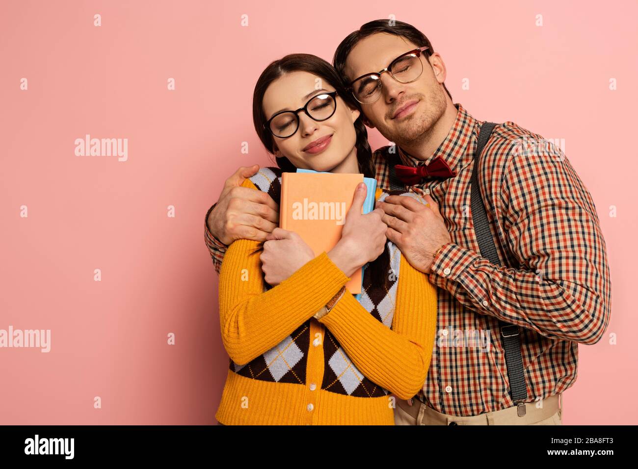 happy nerd with closed eyes hugging girlfriend with books on pink Stock ...