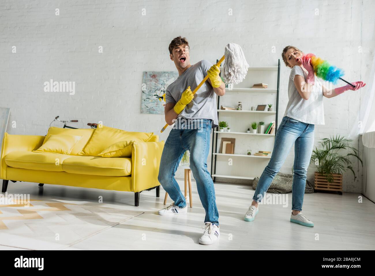 handsome man holding mop and singing with woman while doing spring ...