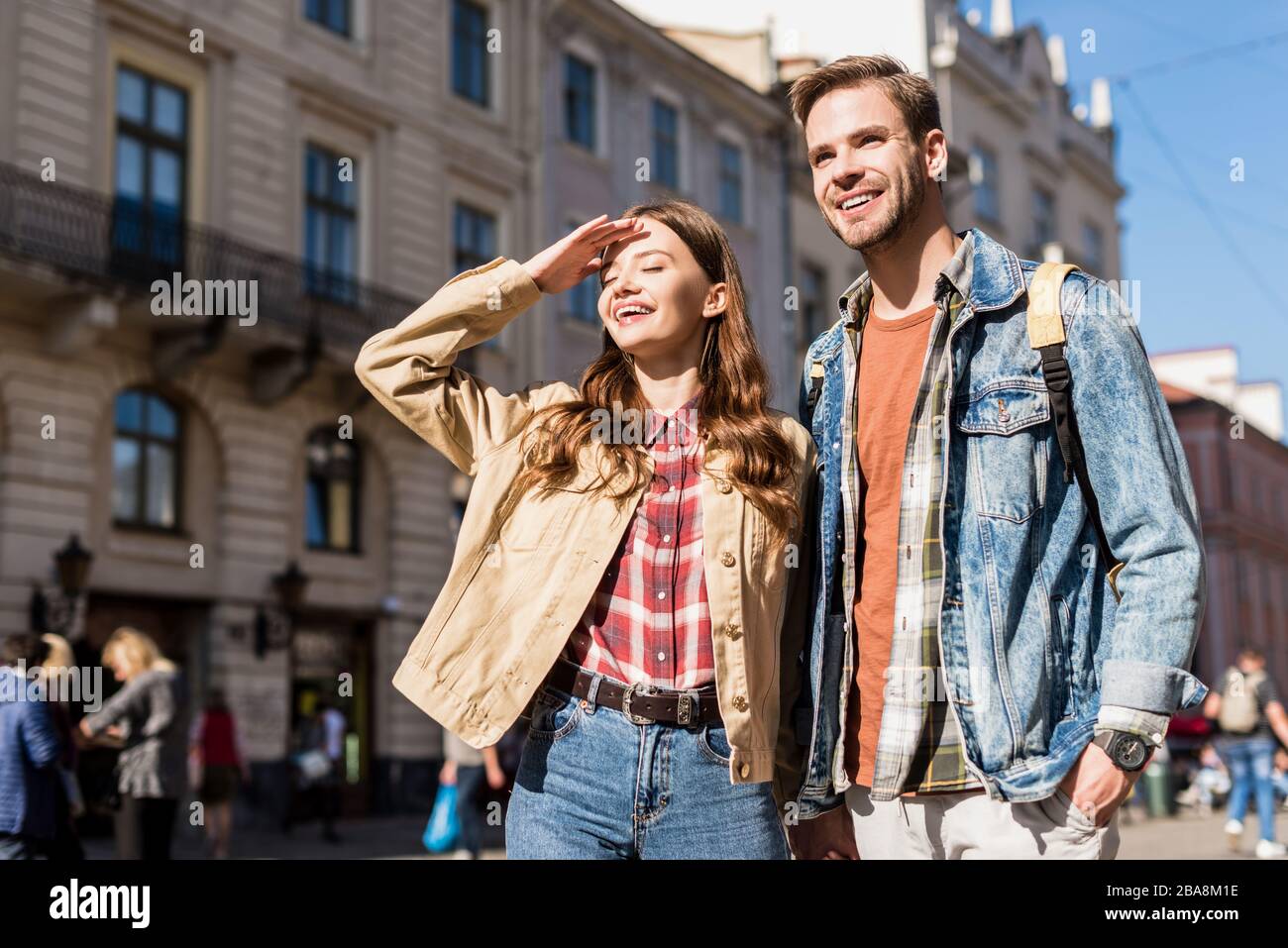 Girlfriend covering face from sunlight and boyfriend smiling in city ...