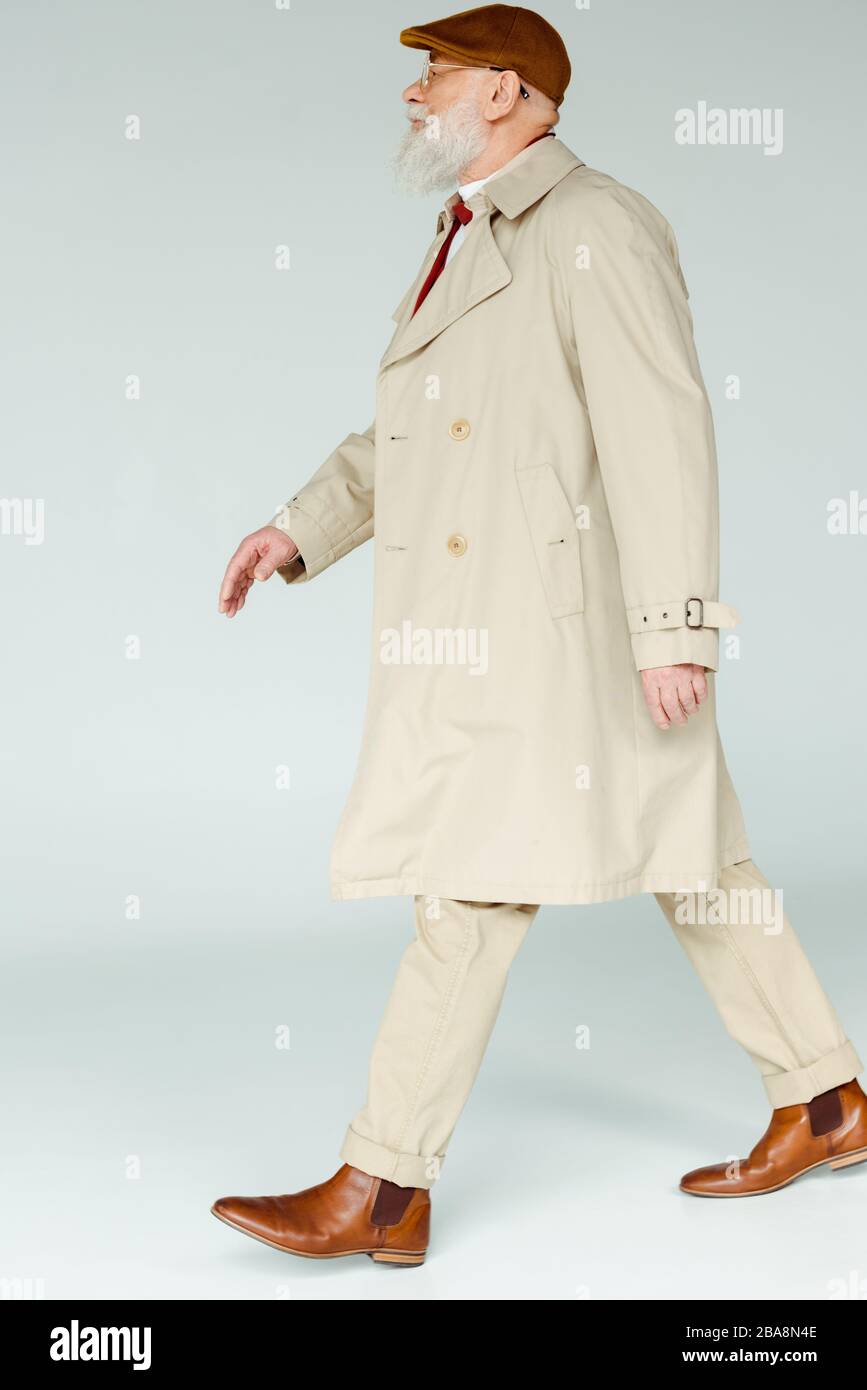 Side view of handsome senior man in coat walking on white background ...