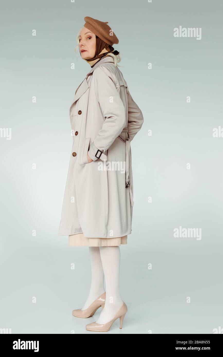 Side view of stylish senior woman in trench coat looking at camera on ...