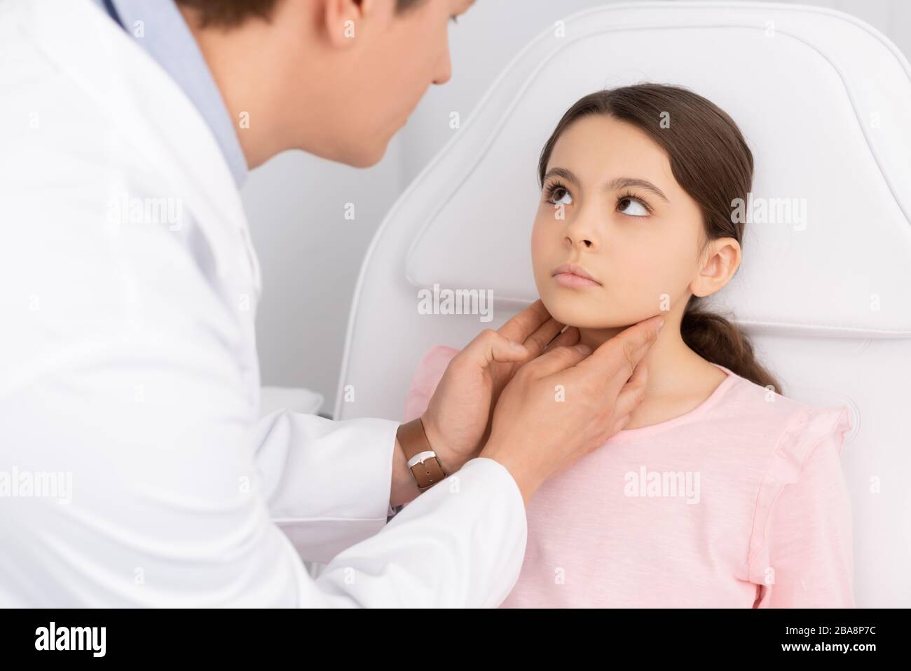 partial view of smiling otolaryngologist touching neck of cute child ...
