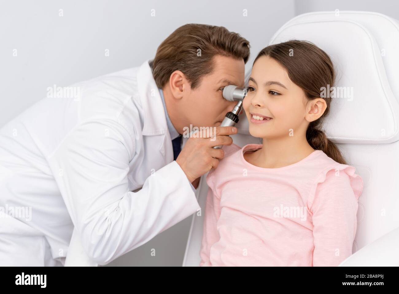 attentive ent physician examining ear of smiling kid with otoscope ...