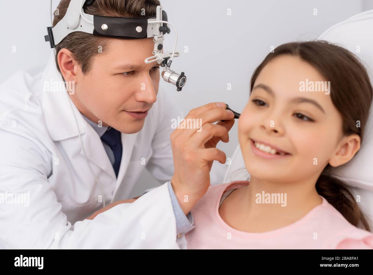 attentive ent physician examining ear of cute child with ear speculum ...