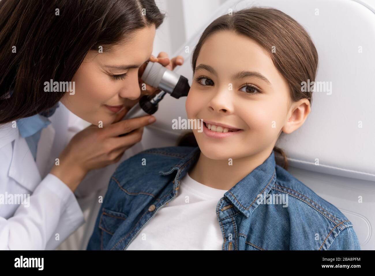 attentive otolaryngologist examining ear of smiling child with otoscope ...