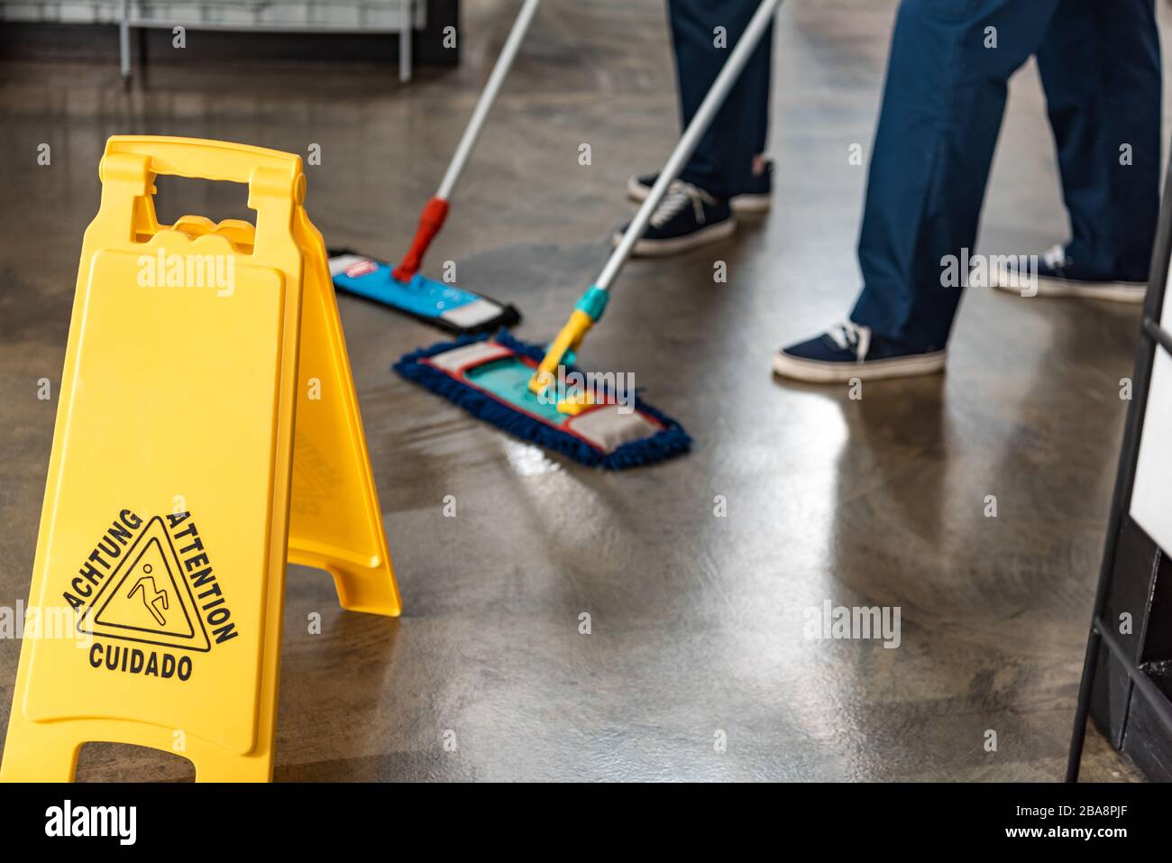partial view of two cleaners washing floor with mops near wet floor ...