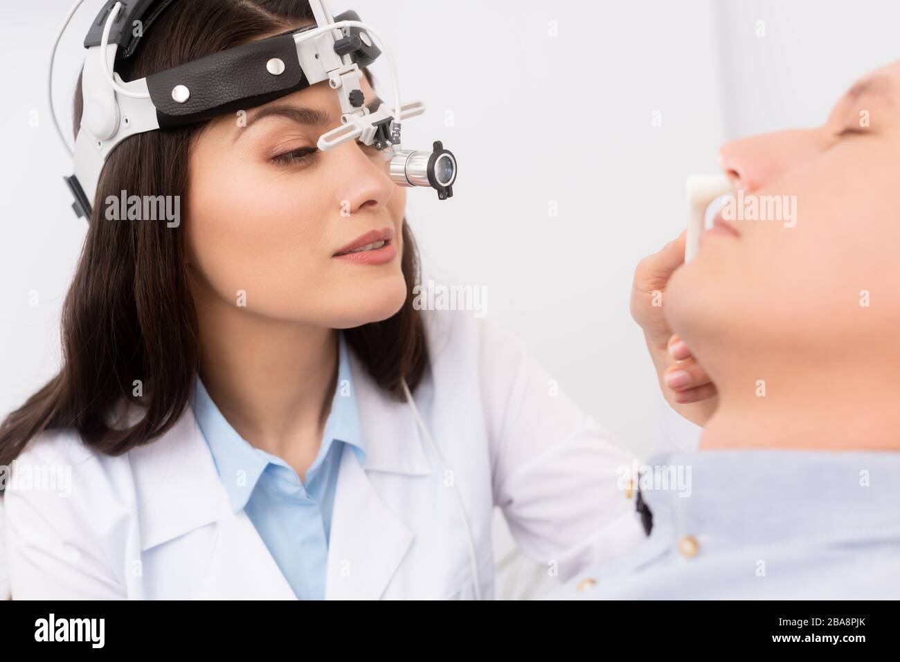 beautiful, attentive otolaryngologist in ent headlight examining nose ...