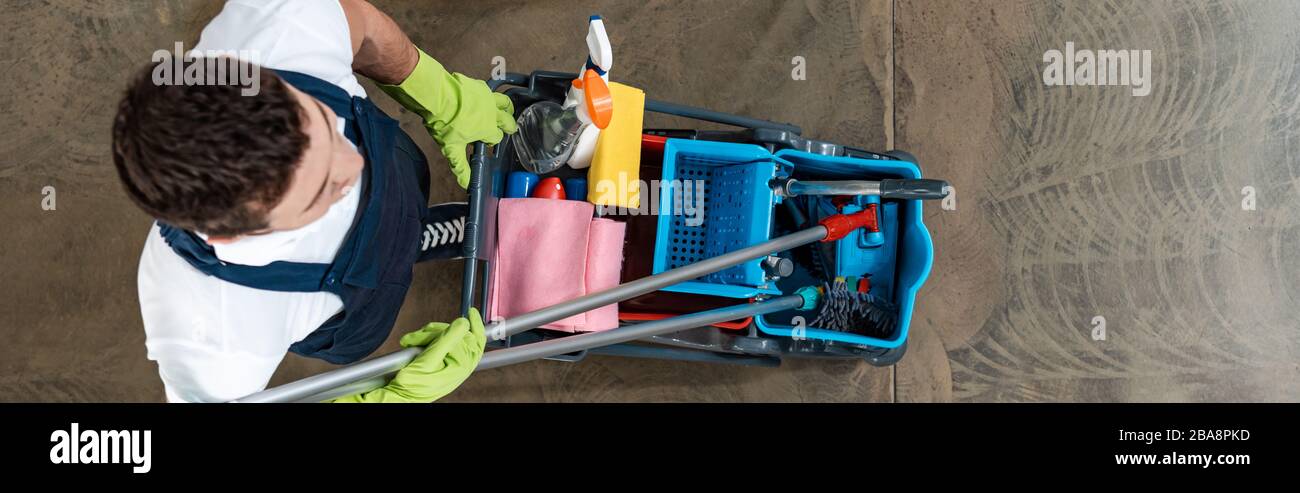 top view of cleaner in uniform carrying cart with cleaning supplies ...