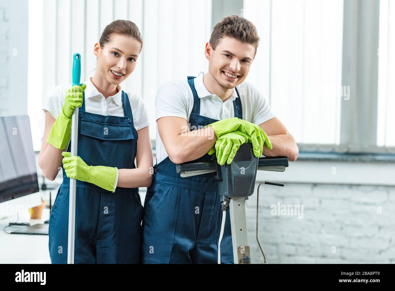 two young cleaners in overalls smiling at camera while standing in ...