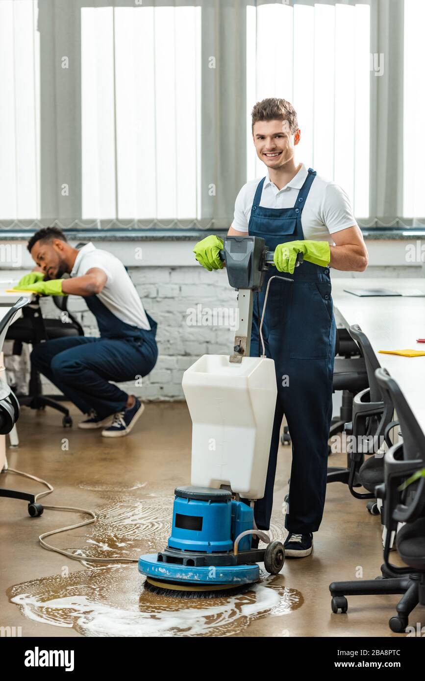 happy cleaner washing floor with cleaning machine while colleague ...