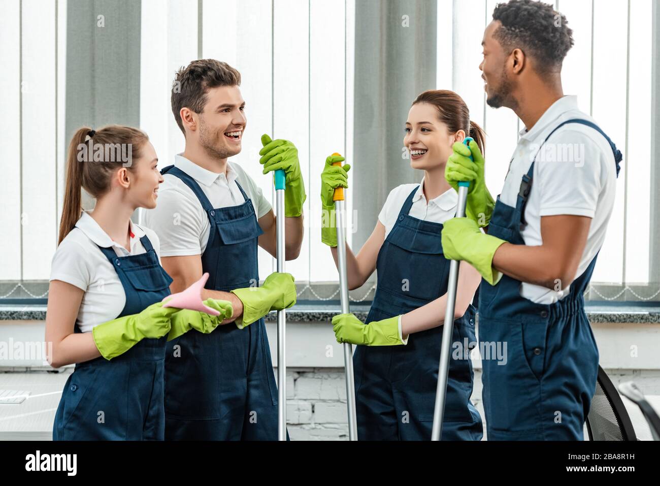 smiling multicultural team of cleaners talking while standing in office ...