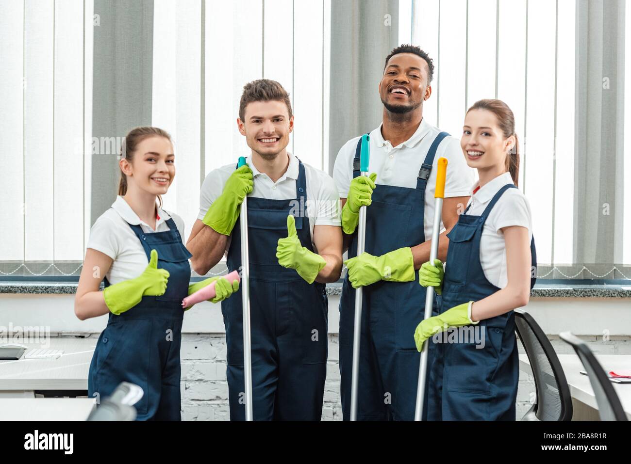 happy multicultural team of cleaners looking at camera and showing ...