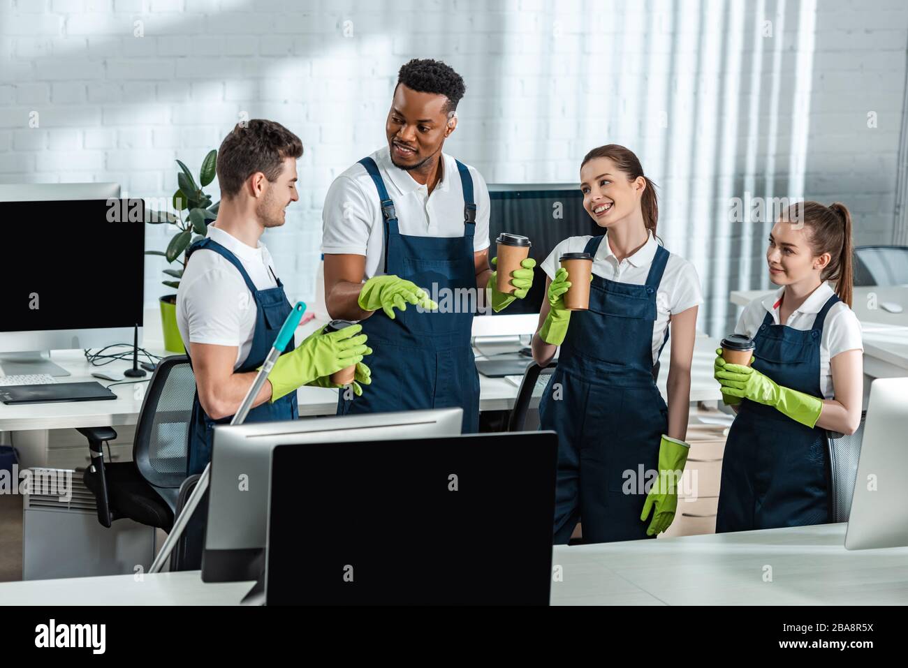 happy multicultural cleaners talking while drinking coffee to go in ...