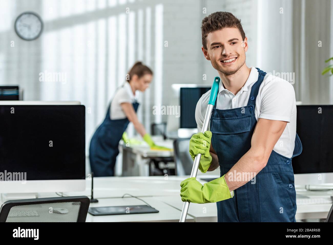 smiling cleaner washing floor while colleague cleaning desk Stock Photo ...