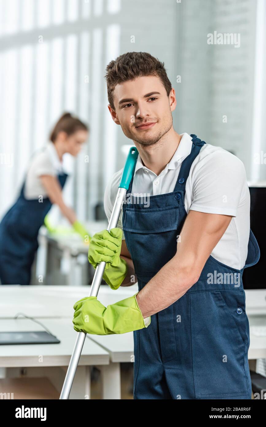 dreamy cleaner looking away while colleague cleaning office desk Stock ...