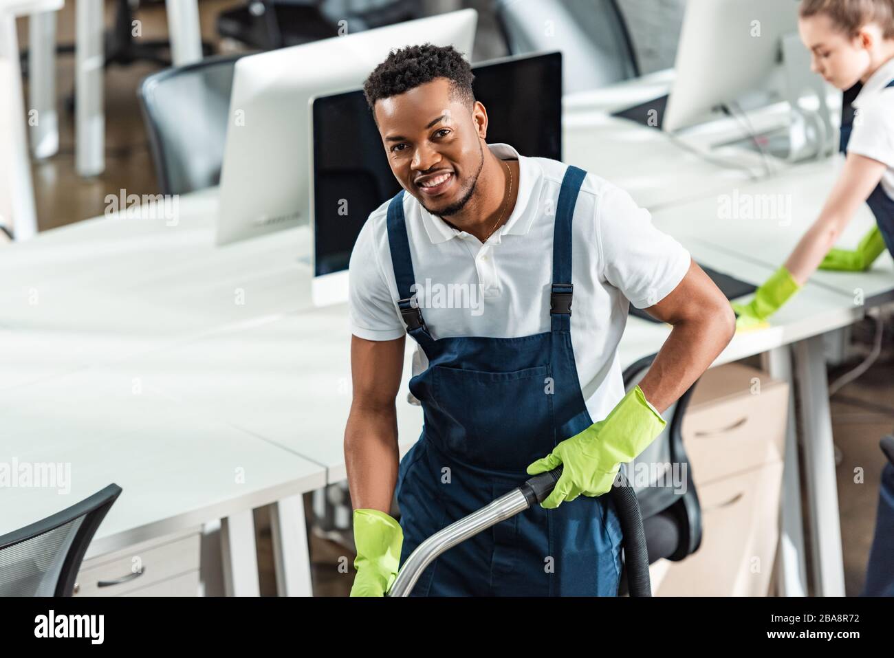 smiling african american cleaner looking at camera near young colleague ...