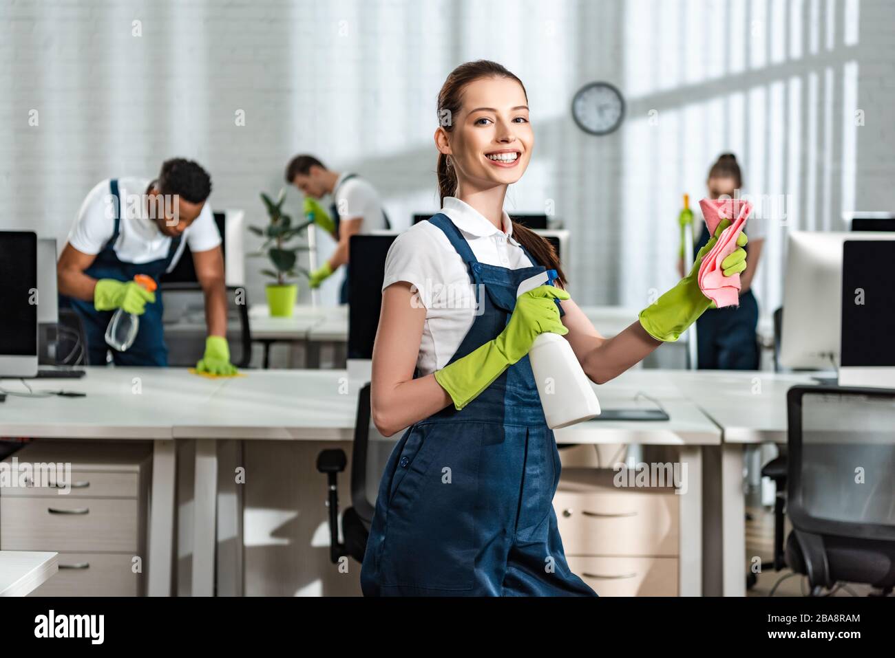 happy cleaner holding detergent spray and rag while standing near ...