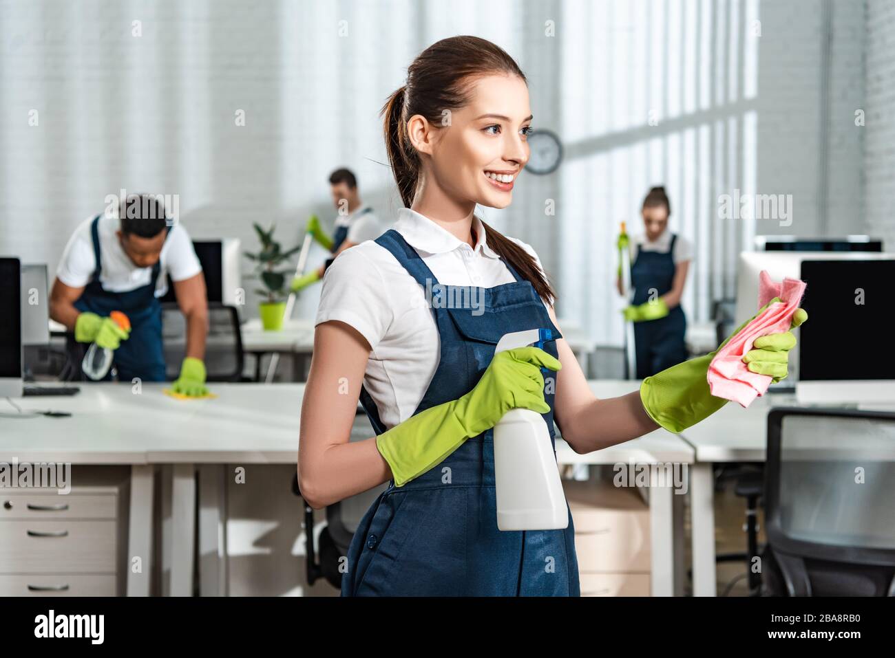 happy, attractive cleaner holding detergent spray and rag while ...