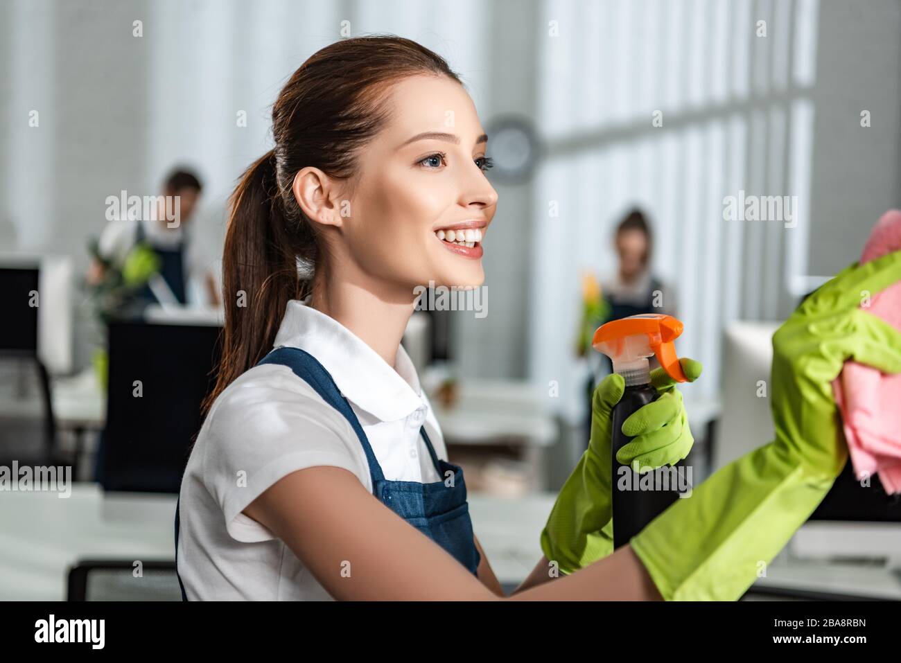 happy, attractive cleaner holding detergent spray and rag while ...