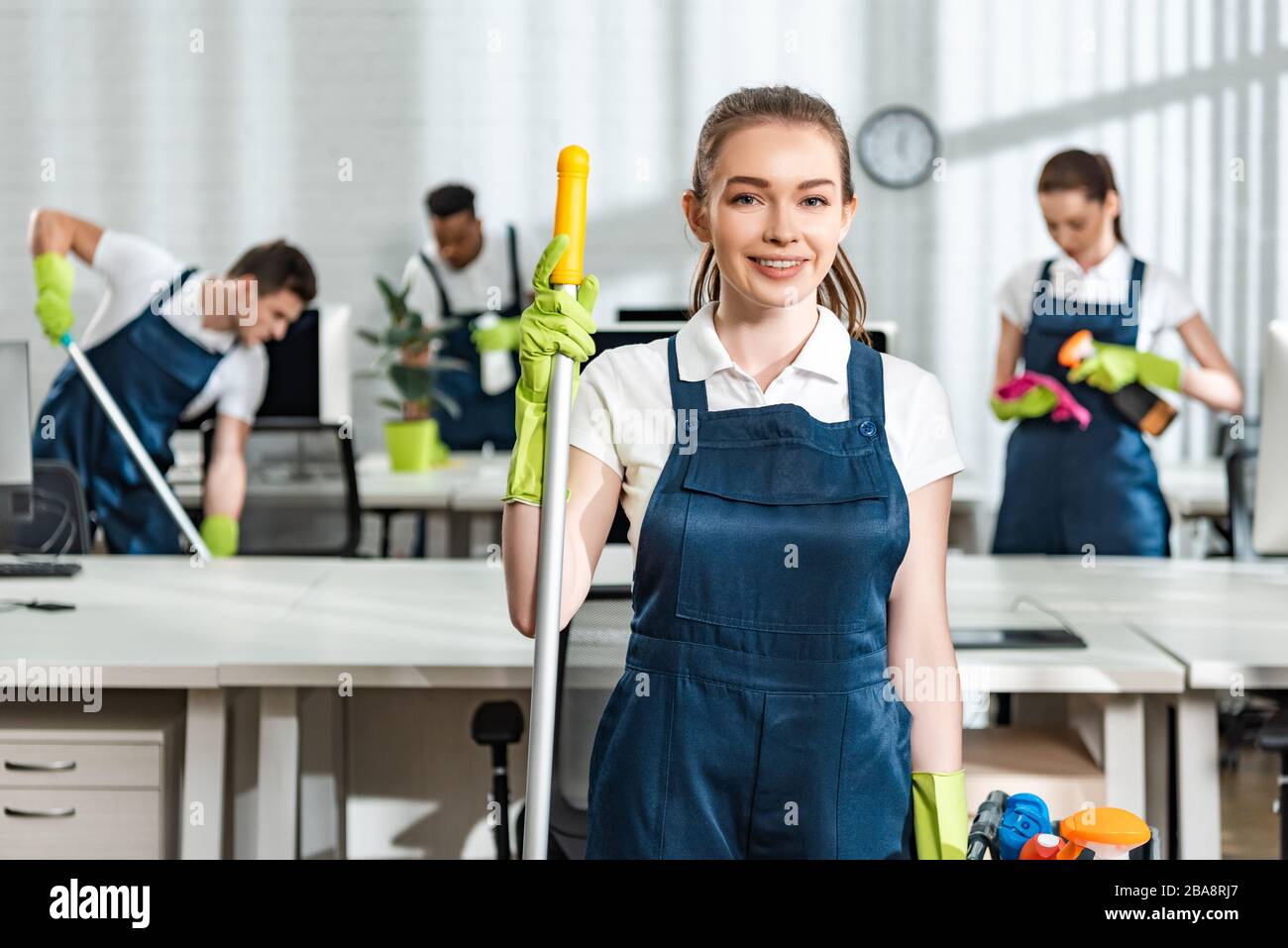 smiling cleaner looking at camera while standing near team of ...
