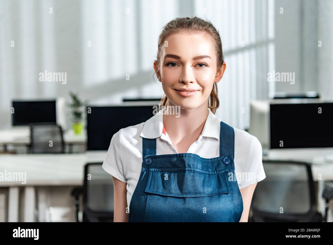 attractive young cleaner in overalls smiling at camera Stock Photo - Alamy