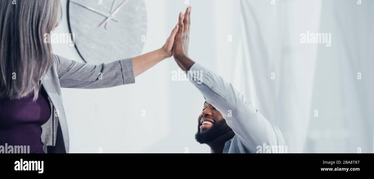 panoramic shot of smiling multicultural colleagues giving high five in ...