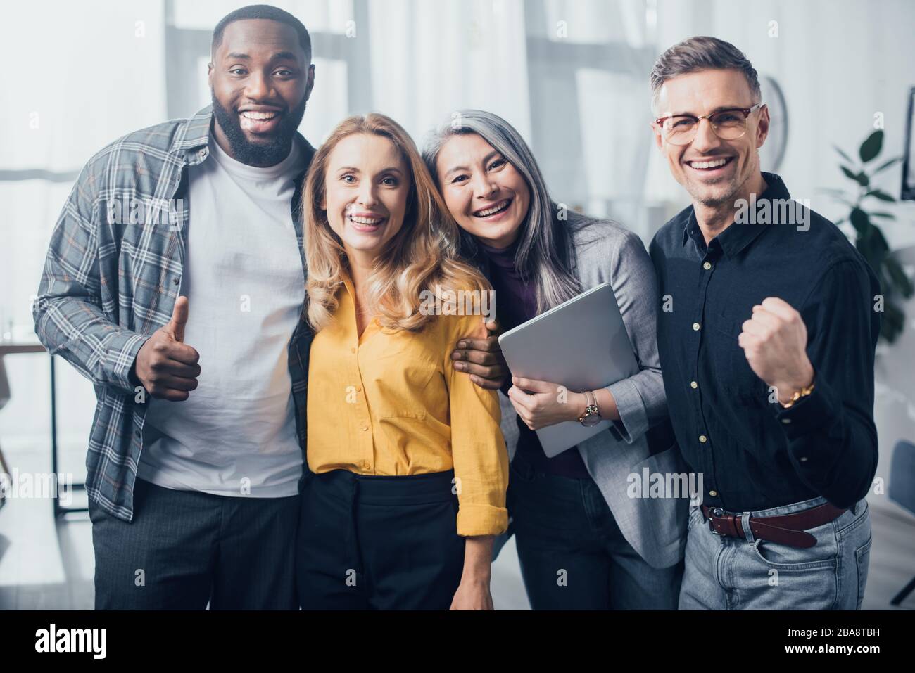 smiling multicultural colleagues hugging and showing like and yes ...