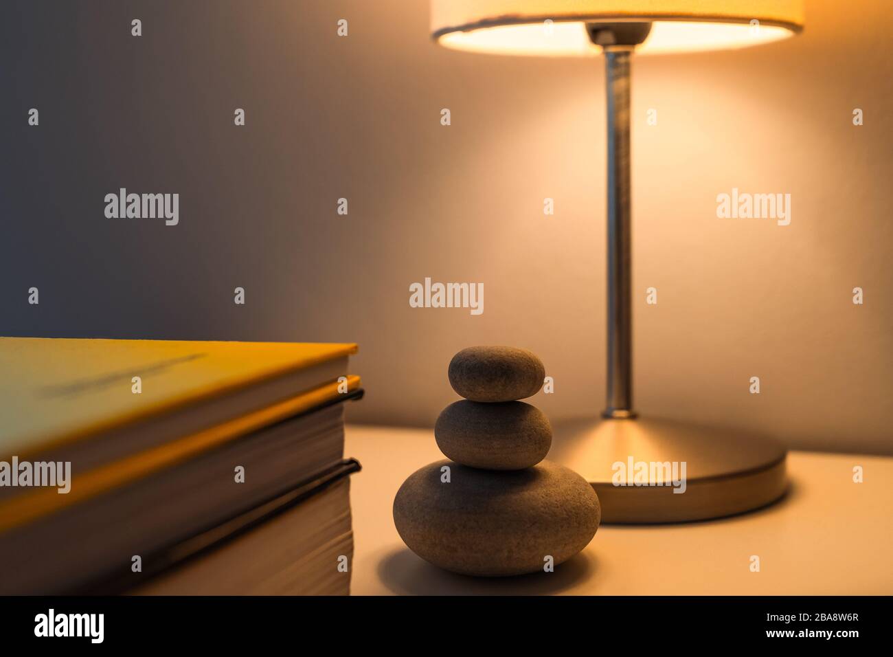 Bedside table with books and a lighted lamp Stock Photo - Alamy