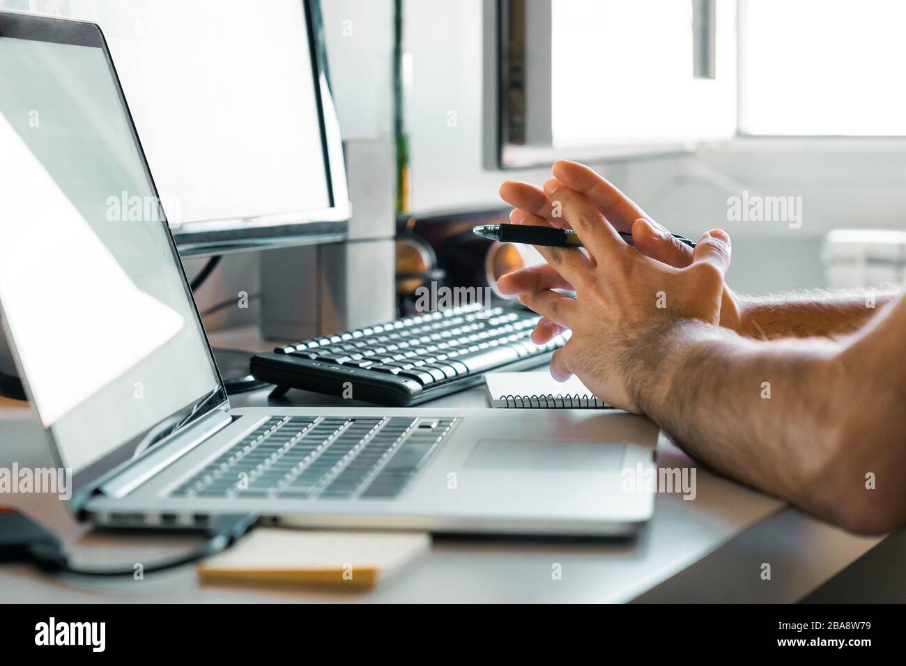 Person holding a pen working from home at their desk with computers ...