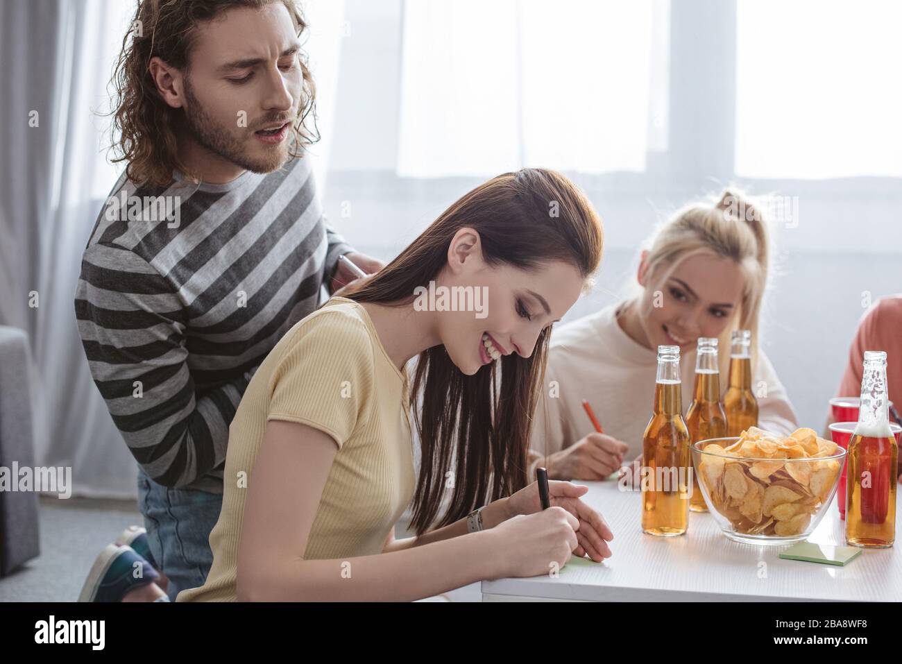 curious man looking at girl writing on sticky note while playing name ...