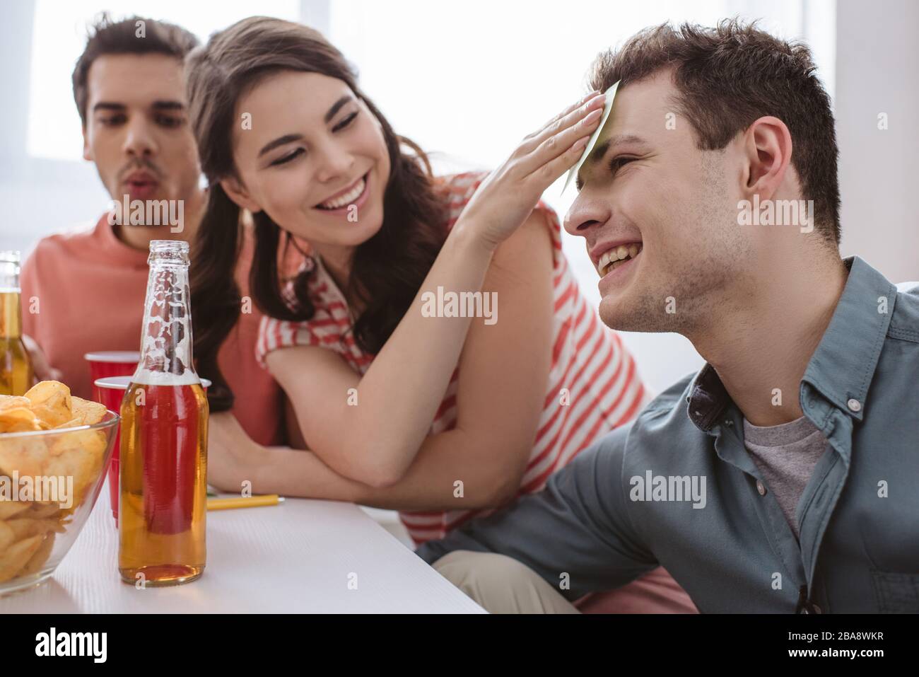 happy girl putting sticky note on forehead of smiling man while playing ...