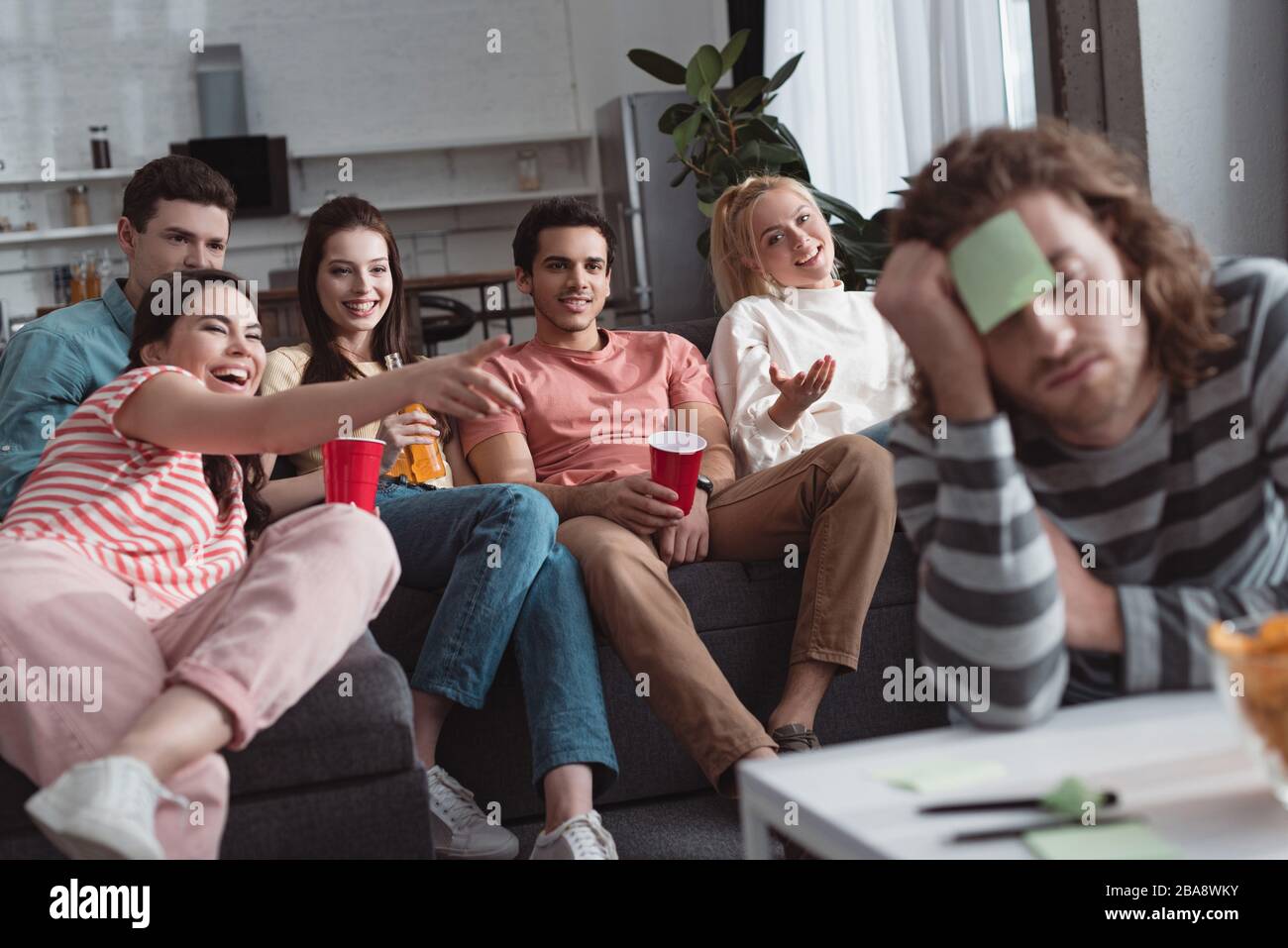 cheerful girl pointing with hand at bored man with sticky note on ...