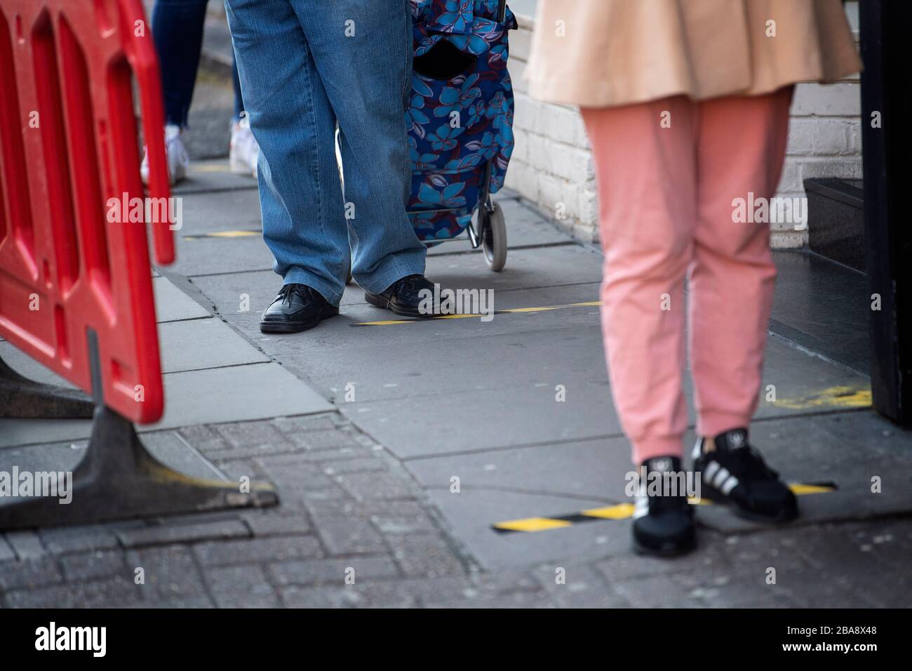 Customers queue between social distancing markers on pavement outside ...