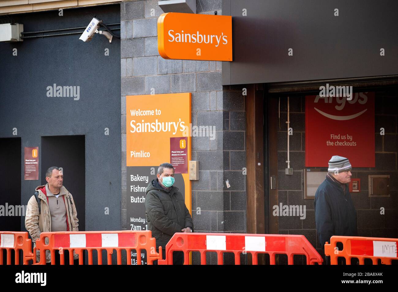 Customers queue between social distancing markers on pavement outside ...