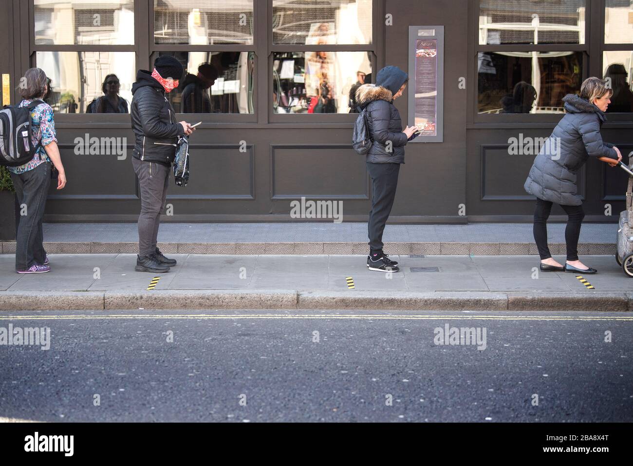 Customers queue between social distancing markers on the pavement ...