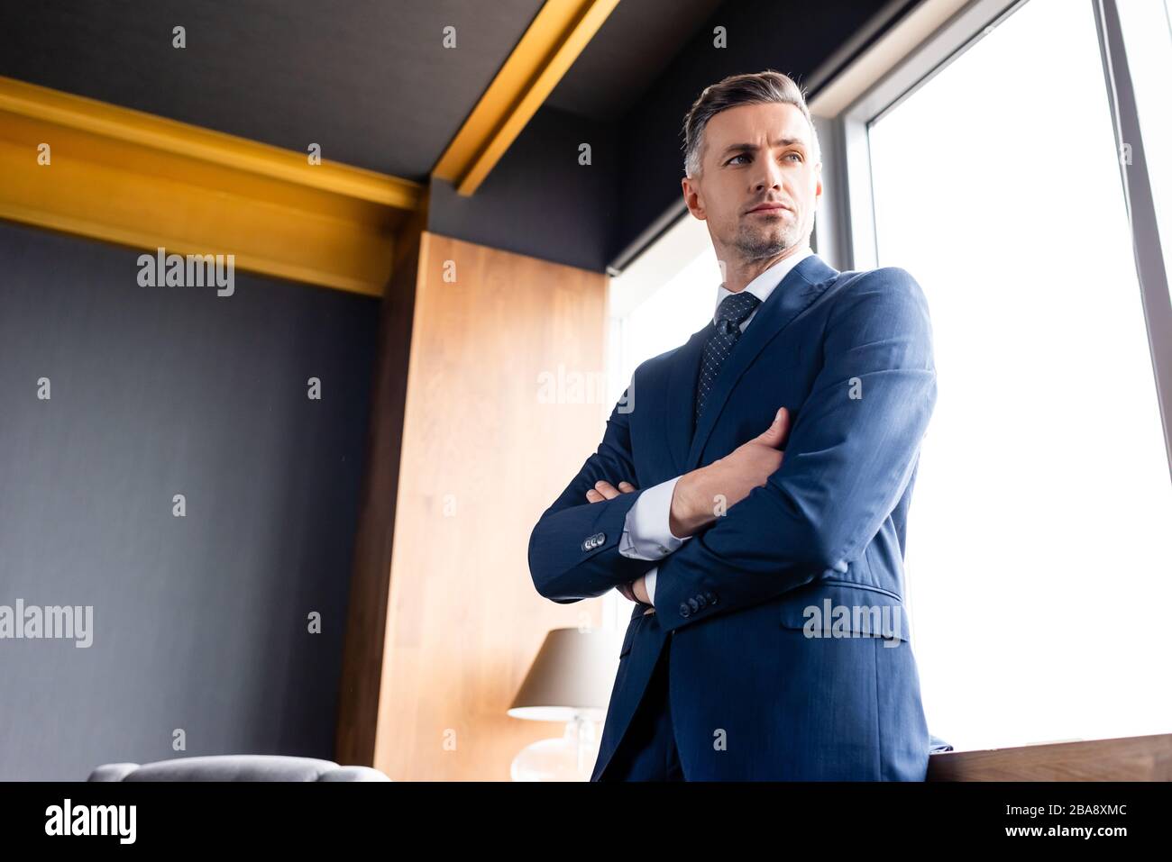 low angle view of businessman in suit with crossed arms looking away ...