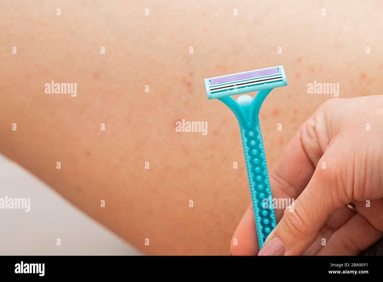 Close up picture of woman holding razor, shaving her hairy leg with ...